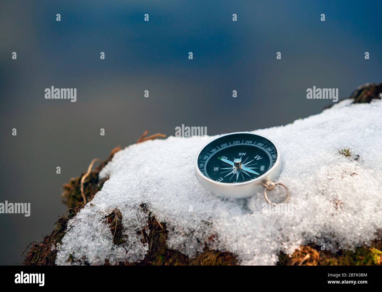 The compass is lying on the snow on the lake shore . The arrow points ...