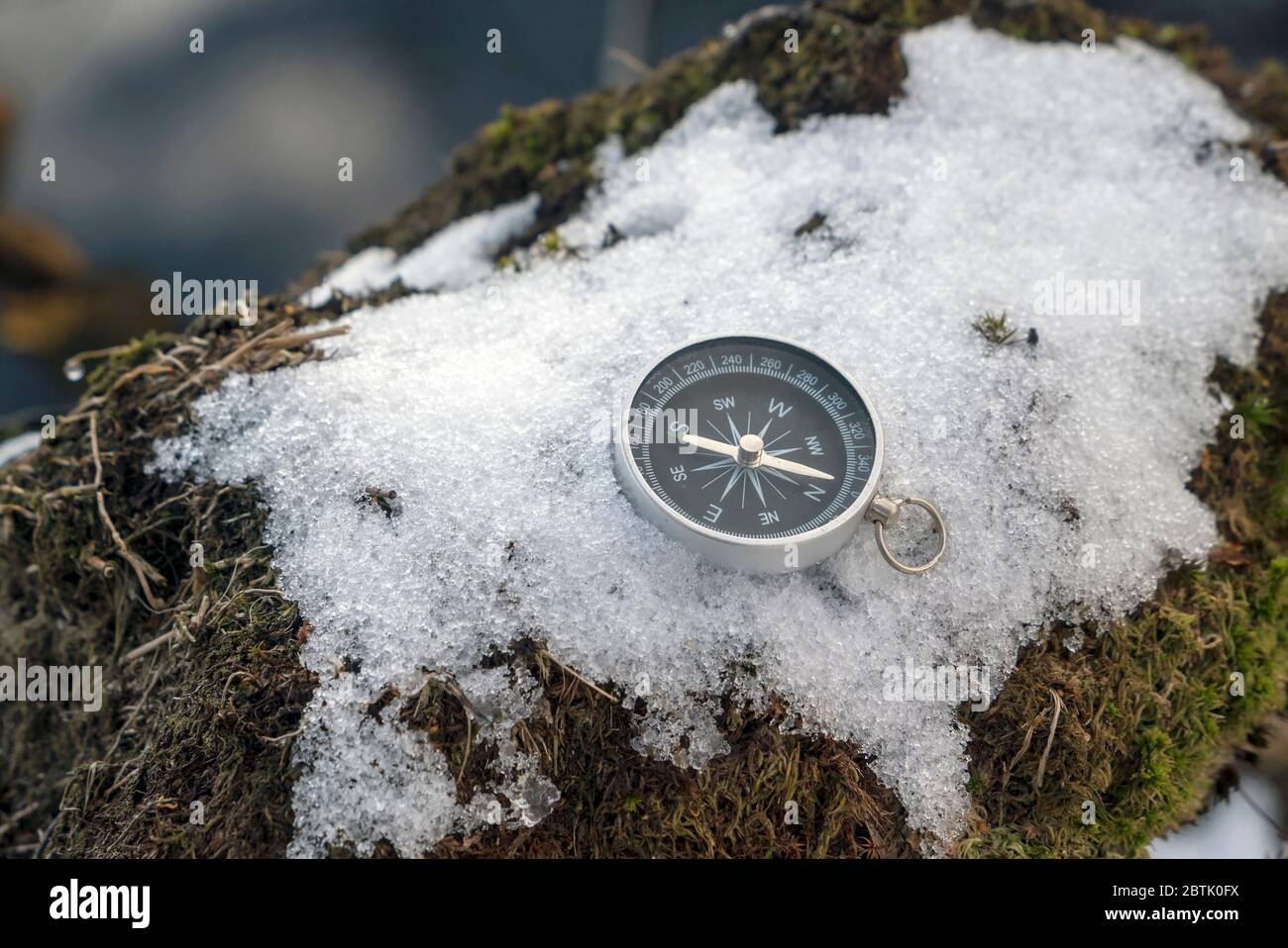 The compass is lying on the snow on the lake shore . The arrow points ...