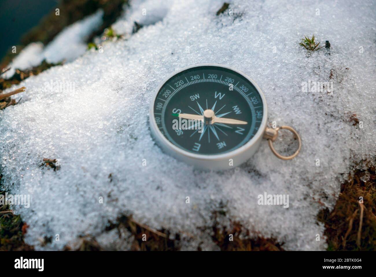 The compass is lying on the snow on the lake shore . The arrow points ...