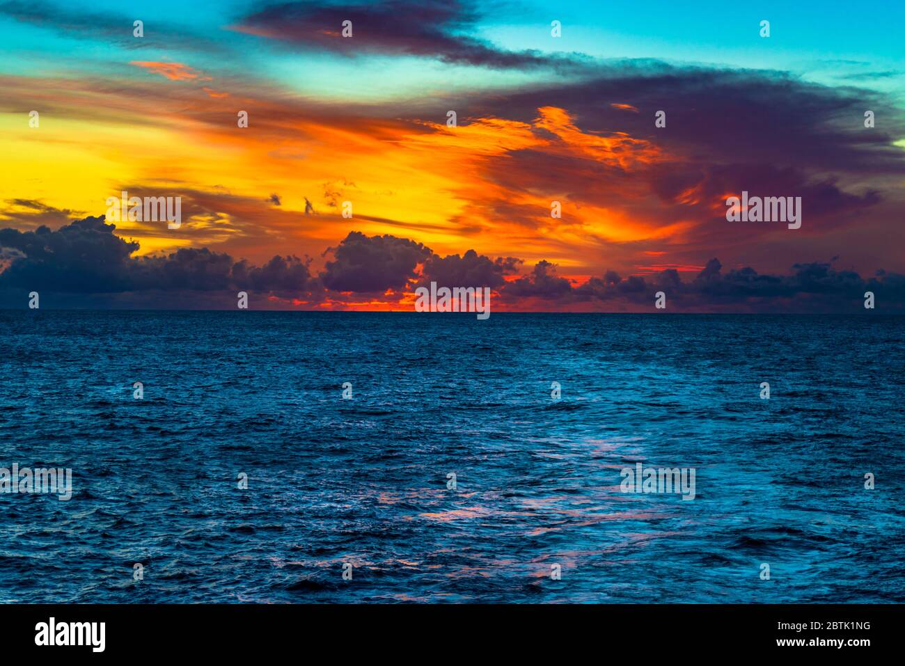 Photo of a spectacular fiery orange sunset over the deep blue waters of ...