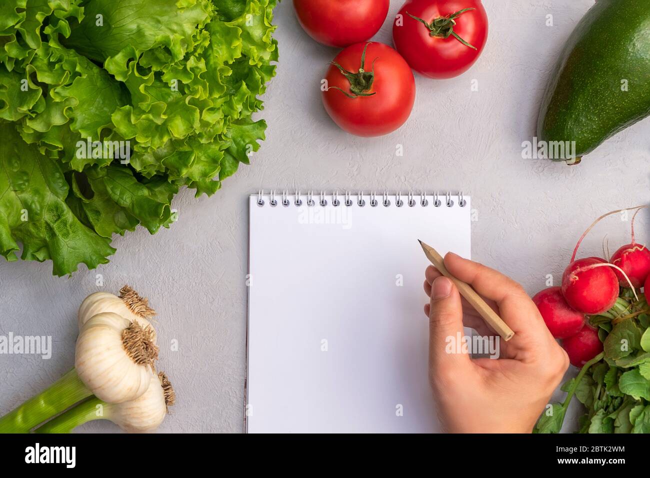 Woman hand holding pencil writing in a paper notepad on kitchen table ...