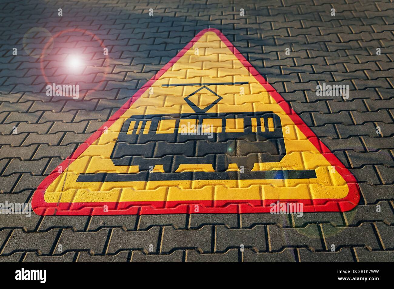 Yellow red triangular tram sign drawn on the road, sun glare effect ...