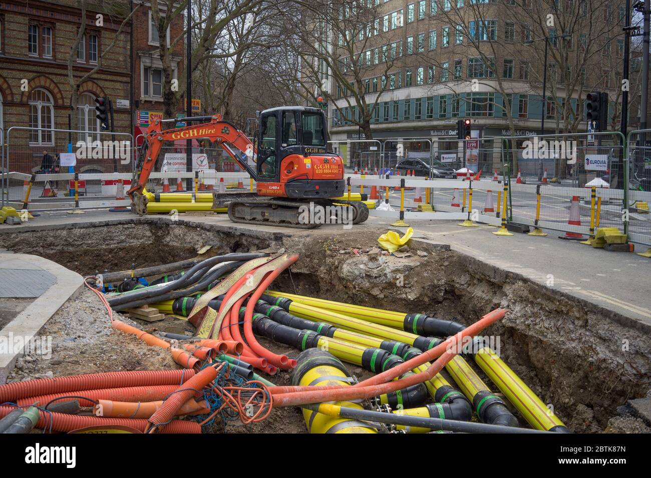 Roadworks with a digger at the side of a large hole with many water ...