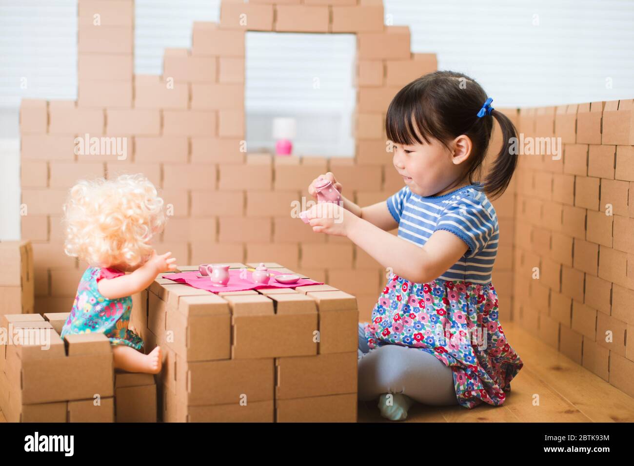 toddler girl pretend play baby care in a cardboard block house Stock ...