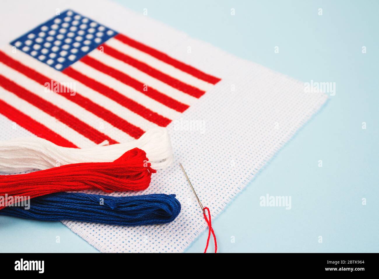 Cross stitch american flag with threads and needle on light blue ...