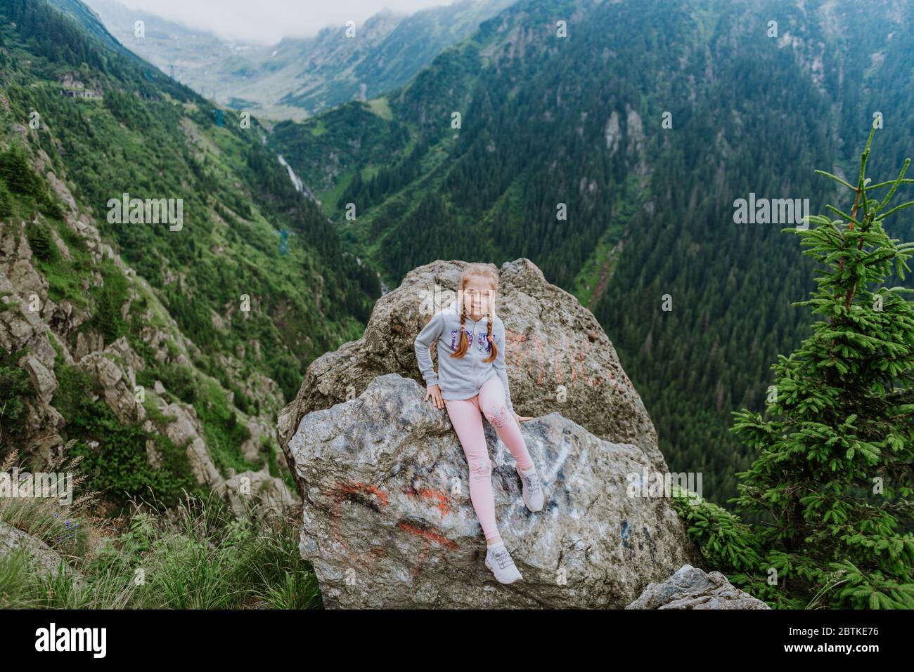 A beautiful girl sits on a rock in the mountains and looks at the ...