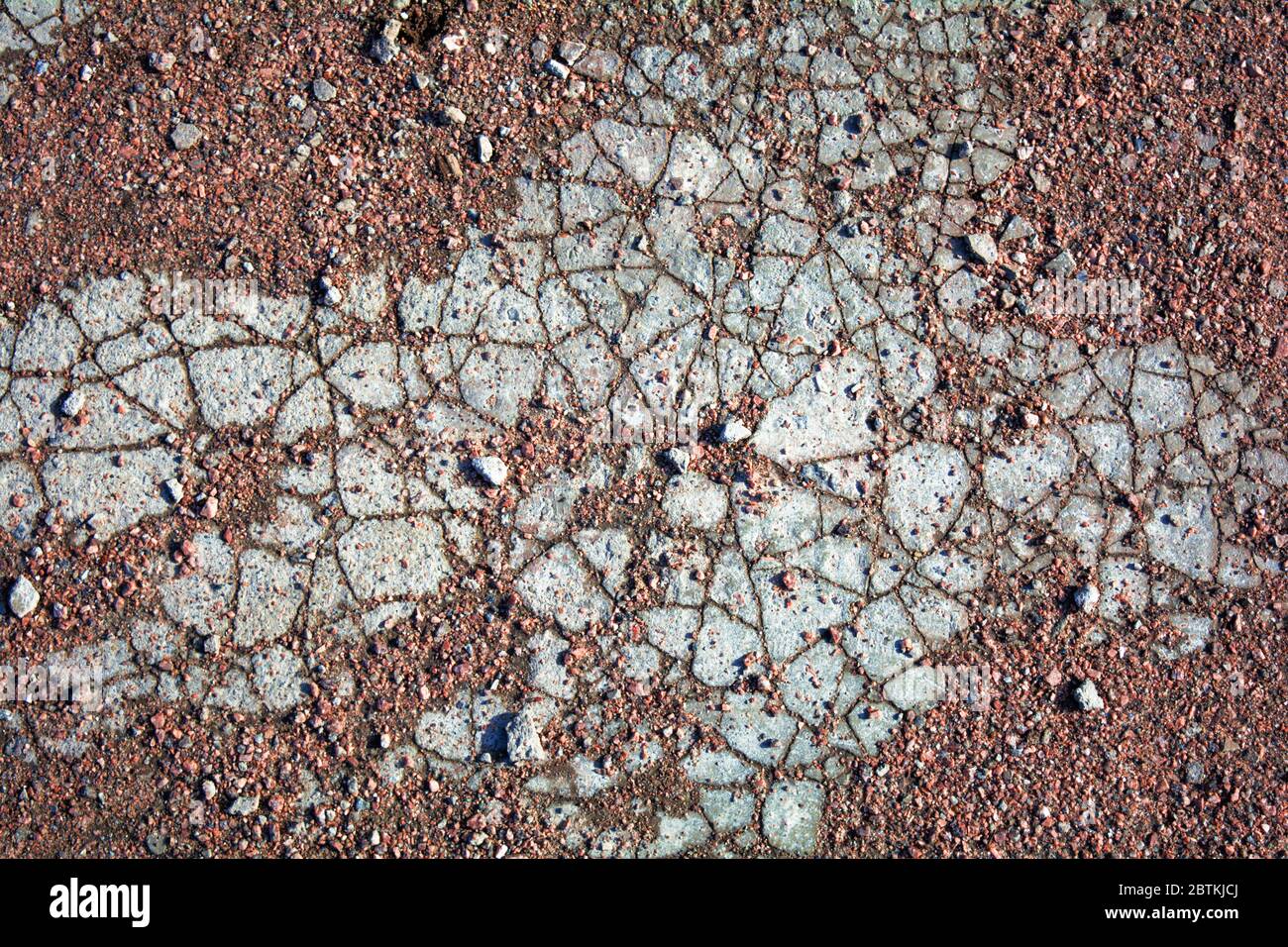 Damaged asphalt pavement road with cracks and red gravel. Ruined urban ...