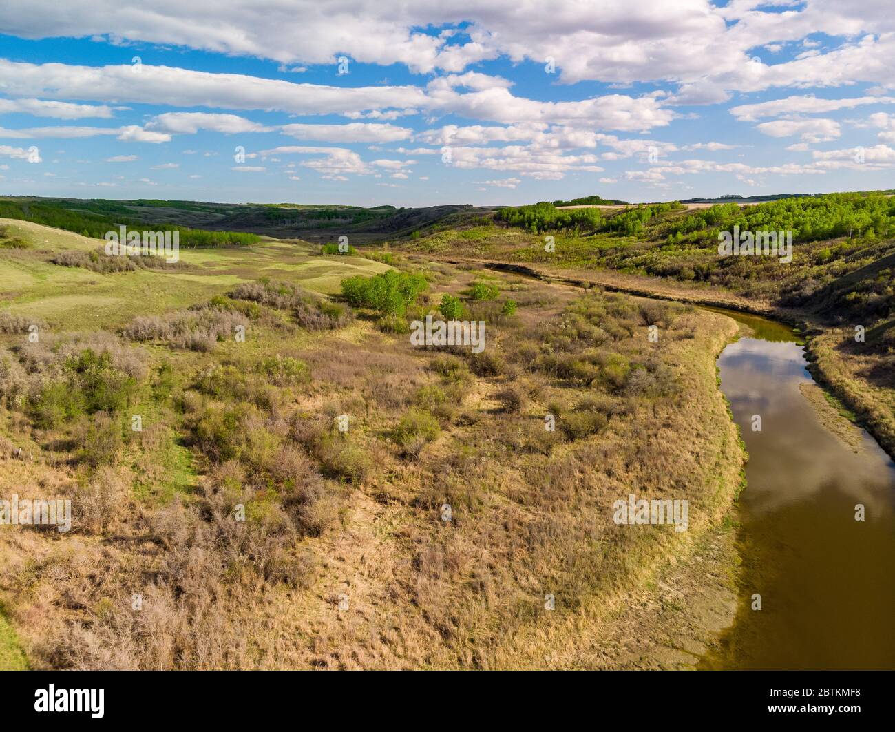 An aerial view of a calm stream running through a valley in the prairie ...