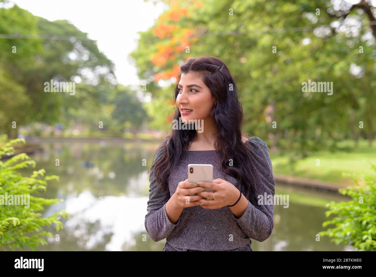Happy young beautiful Indian woman thinking while using phone at the ...