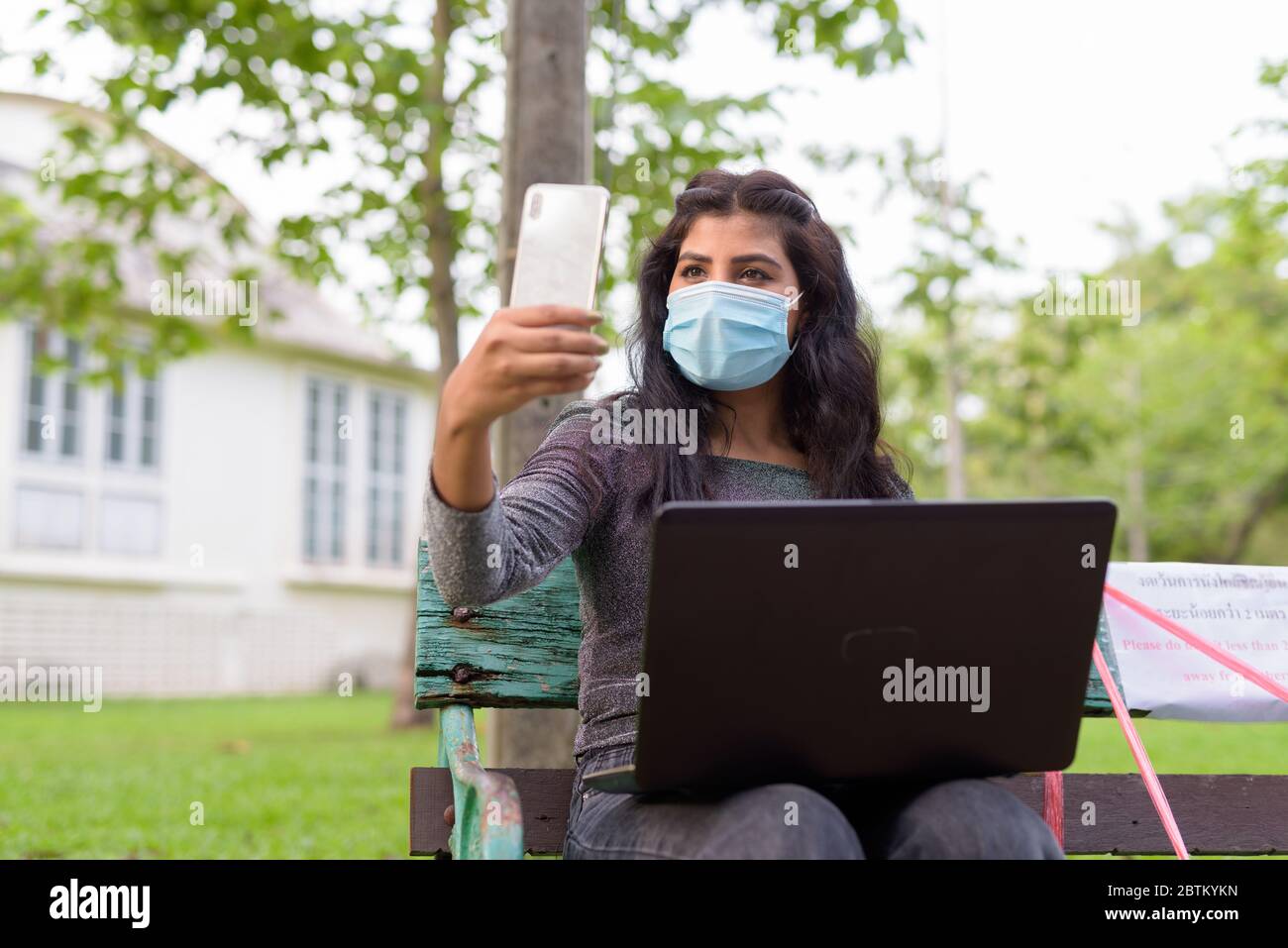 Young Indian woman with mask video calling using phone while sitting ...