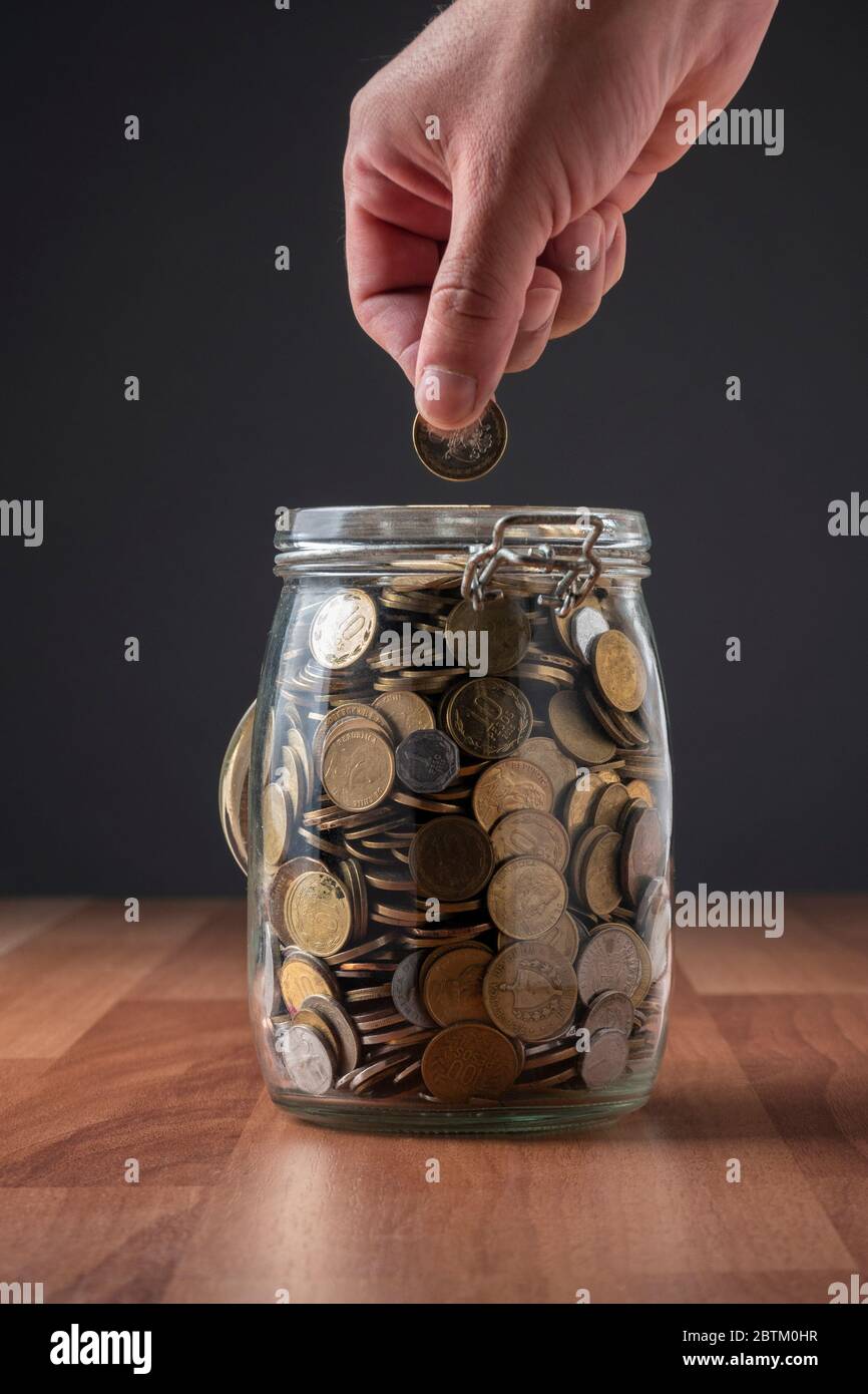 A person putting coins in a container full of money Stock Photo - Alamy