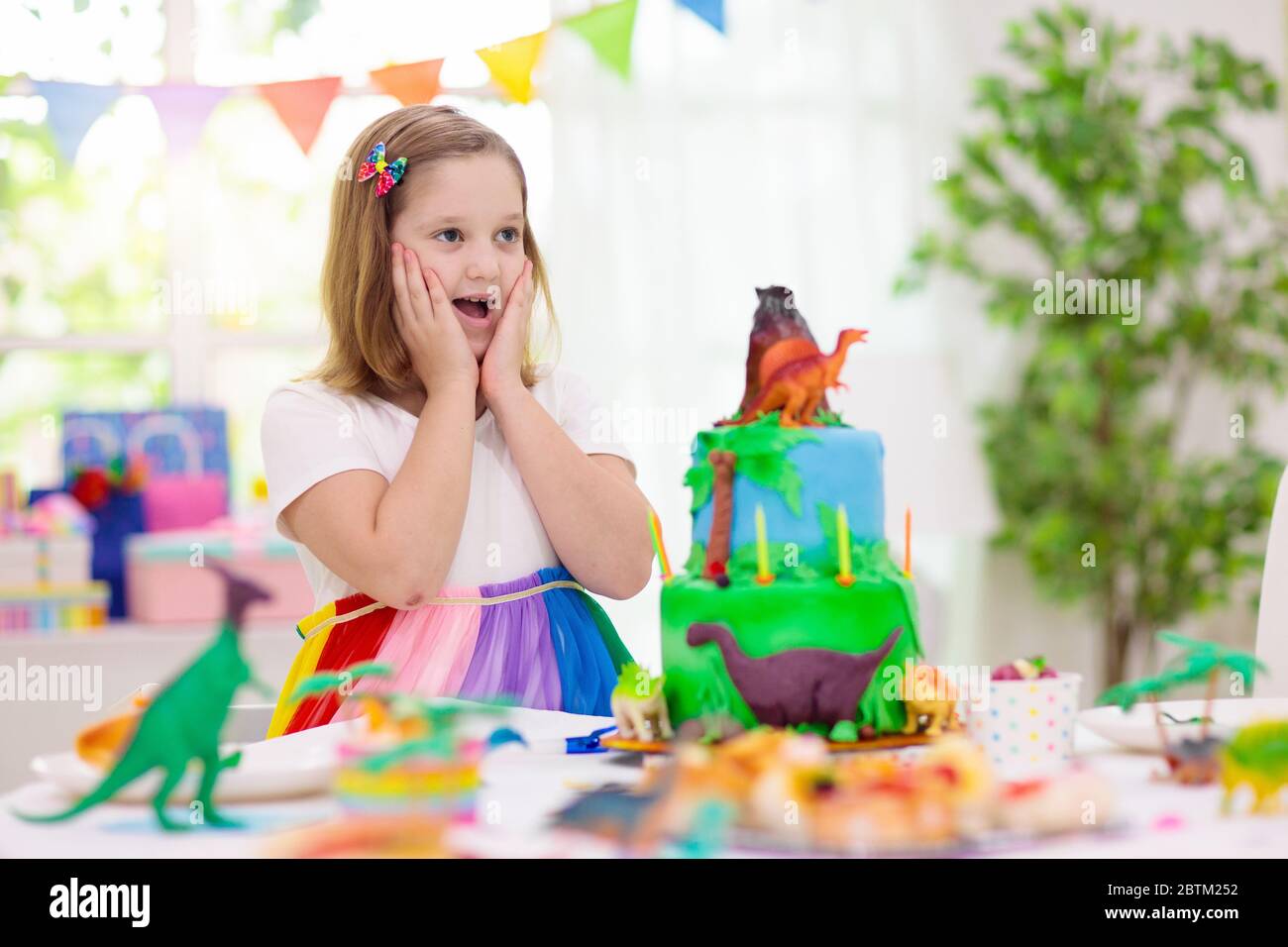Kids birthday party. Dinosaur theme cake. Little girl blowing candles ...