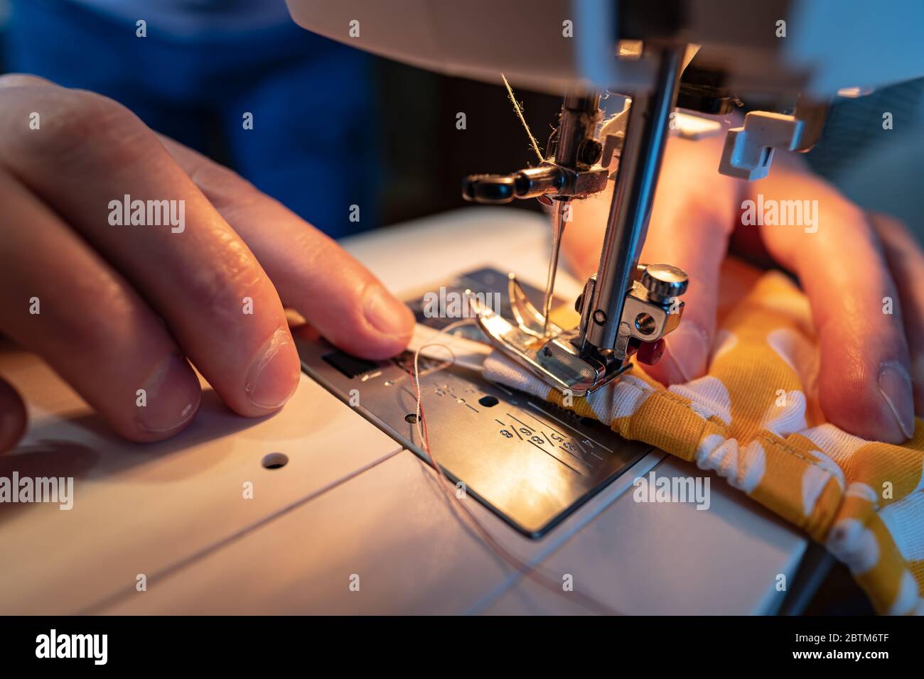Male hands sew a protective mask using a modern electric sewing machine ...