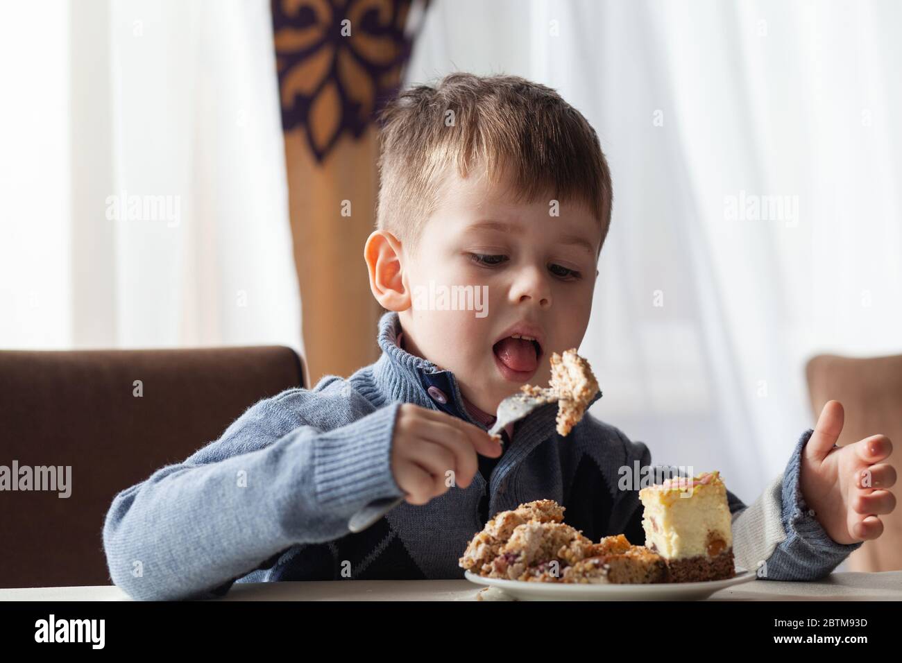 Cute little boy in cafe eat a big piece of cake with a fork. Desserts ...