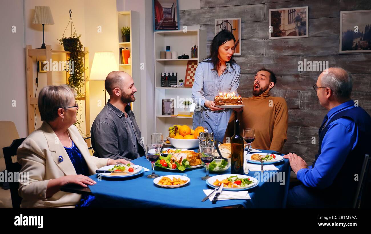 Follow shot of young woman with birthday cake for her brother at family ...