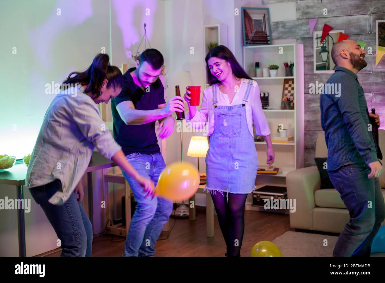 Cheerful young man holding a beer bottle while dancing with his friends ...