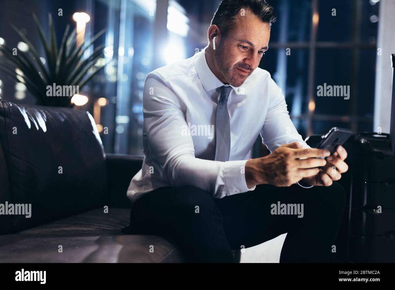 Businessman sitting at airport executive lounge using his mobile phone ...