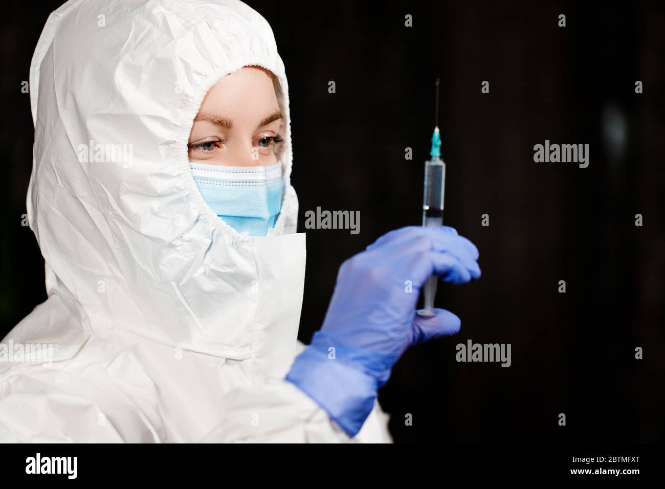 Healthcare medical doctor in protective medical suit looks at syringe ...