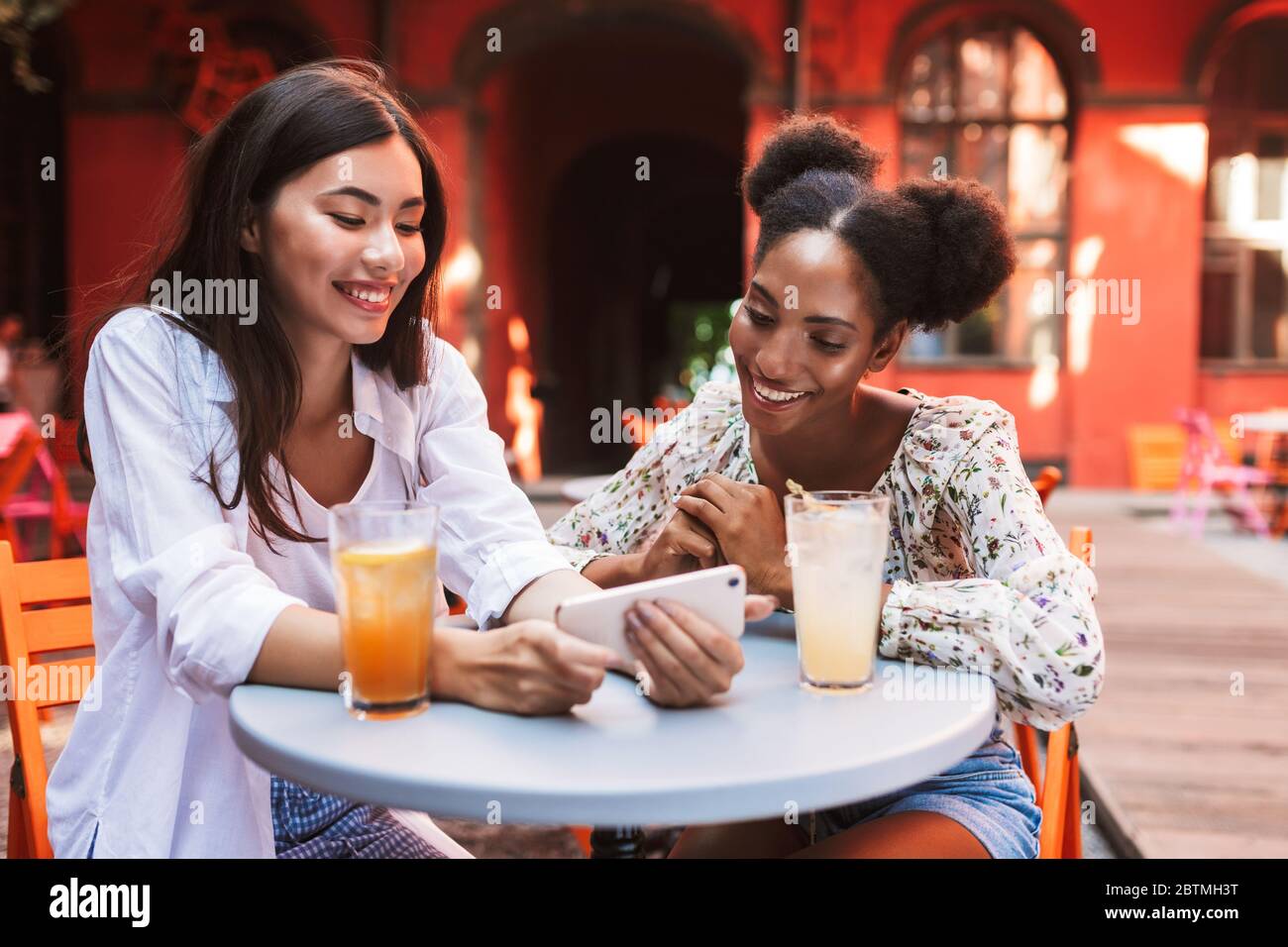 Two beautiful ladies happily using cellphone together with drinks near ...