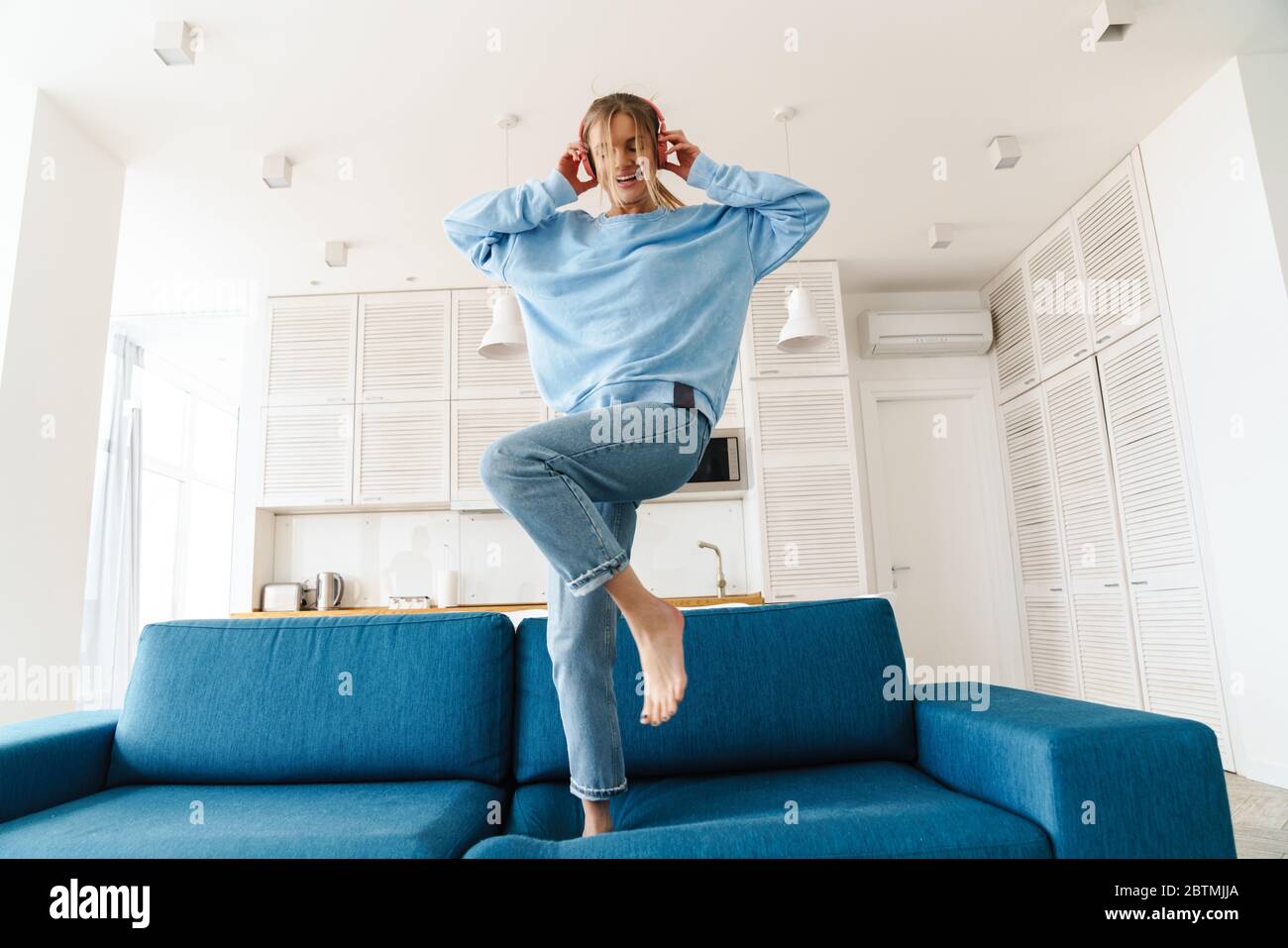 Image of cute smiling woman dancing on couch while using wireless ...