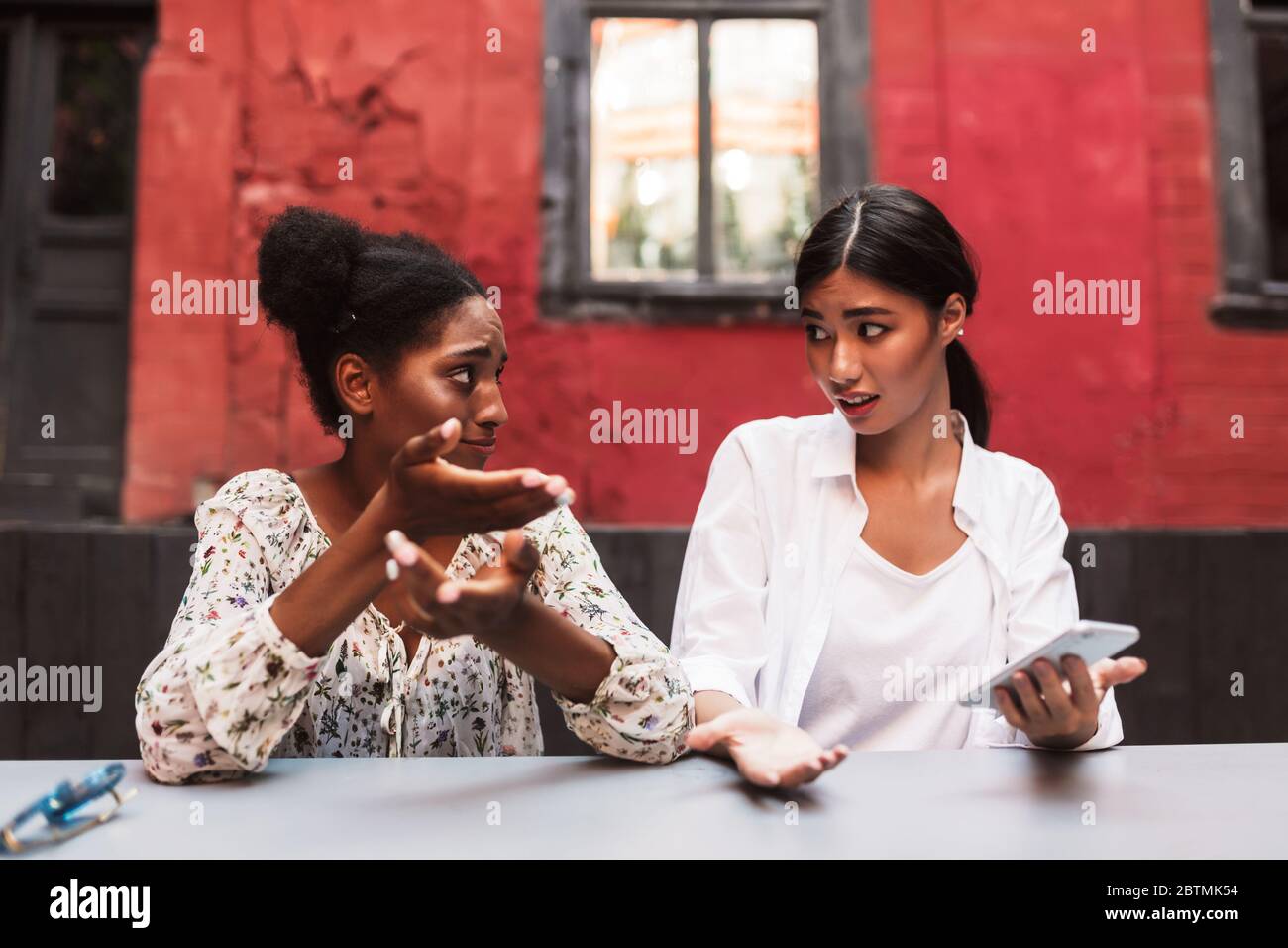 Two young women amazedly looking at each other while spending time ...