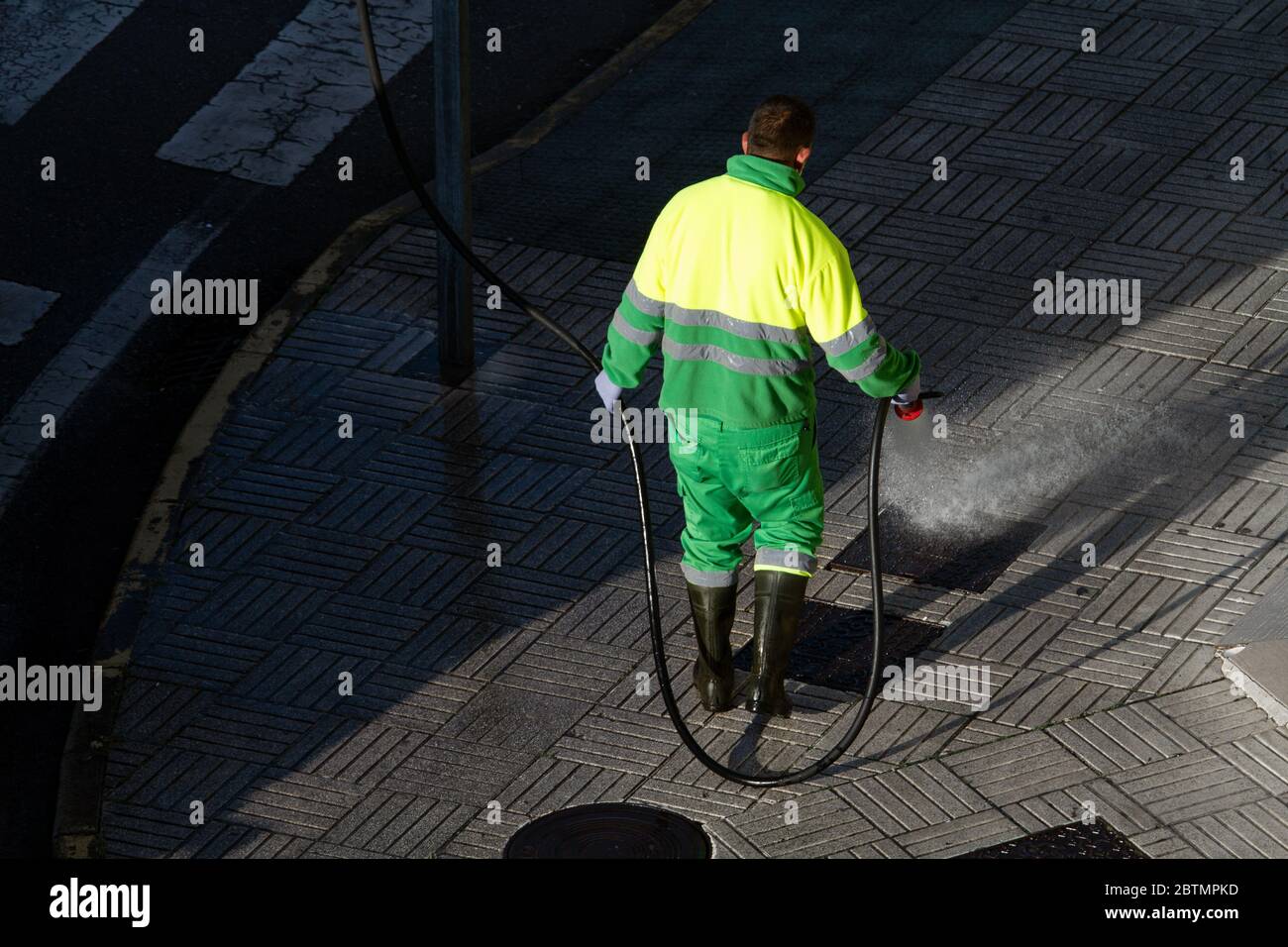 Worker holding a hose cleaning the sidewalk with water. Urban ...