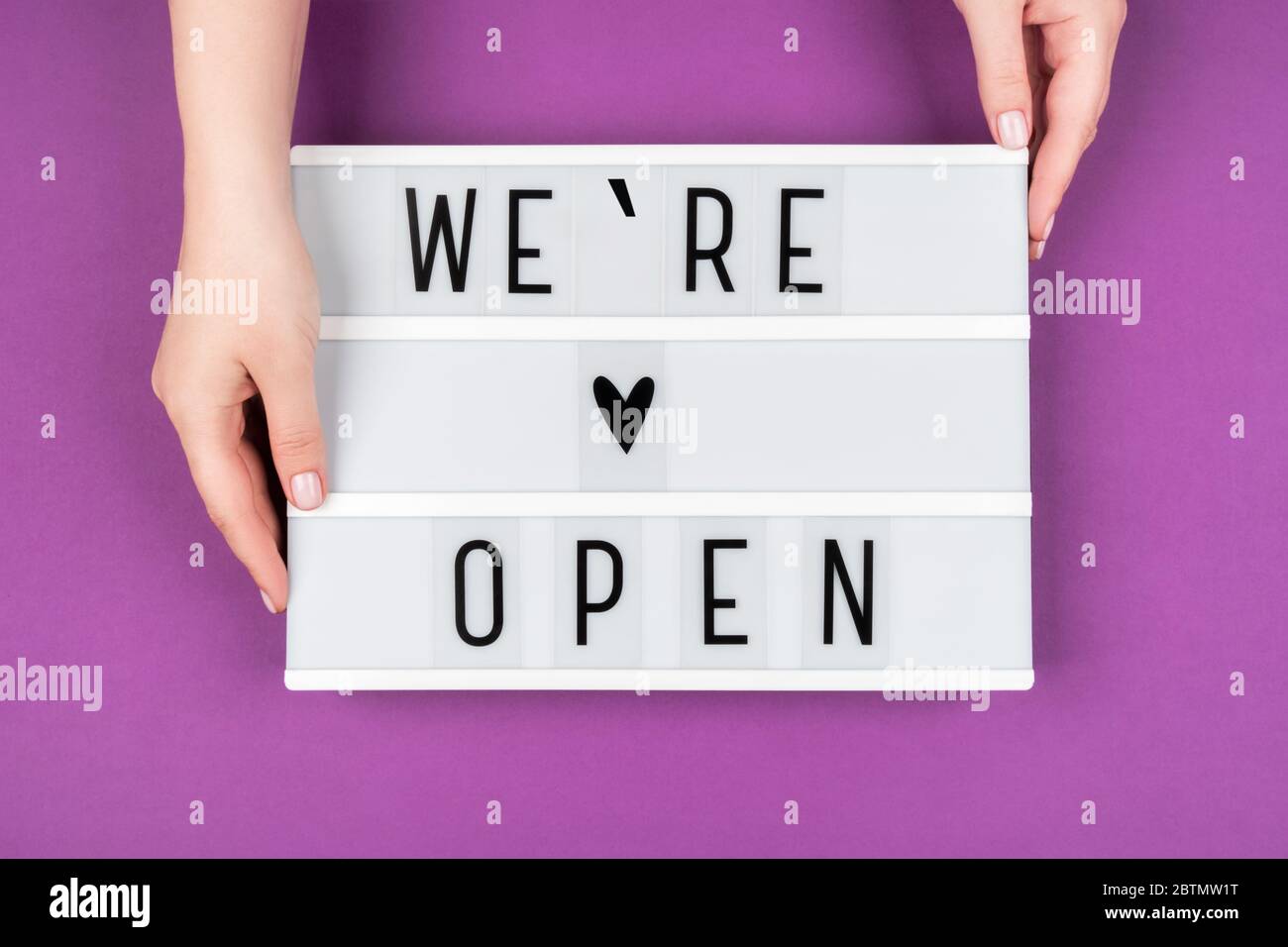 We're open text on a lightbox on a purple background in women's hands ...