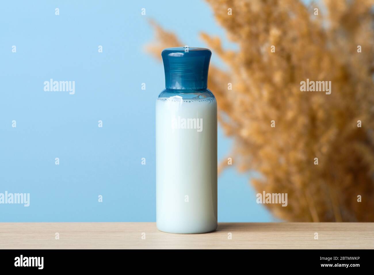 Clear cosmetic bottle with milk moisturizer lotion on blue background ...