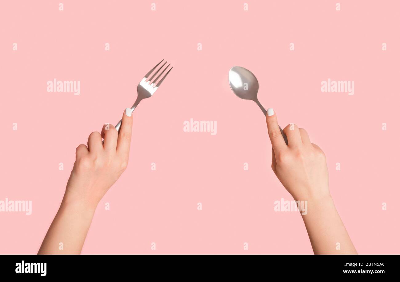 Closeup of female hands holding metal spoon and fork against pink ...