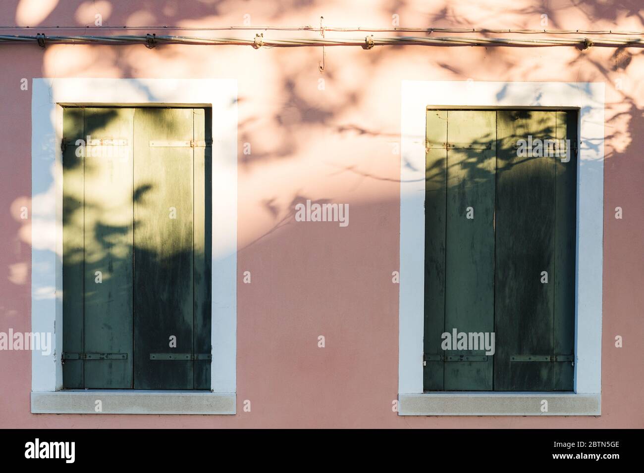 Concrete wall with closed shutters on windows and trees shadows ...