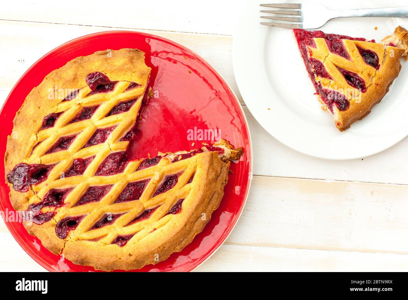 Blueberry lattice pie on a red plate with a slice on a white plate with ...