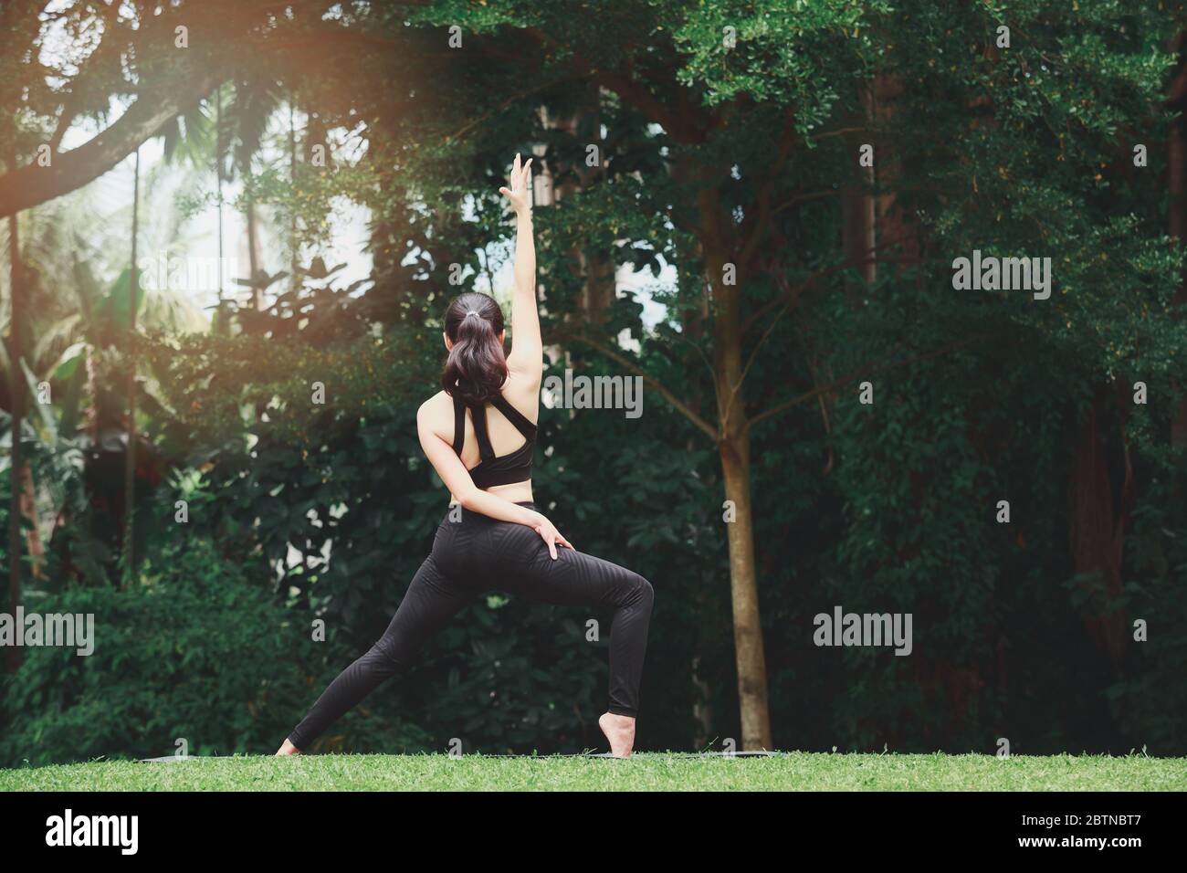 Asian woman practicing yoga in Warrior Pose (Virabhadrasana) on the mat in outdoor park Stock ...