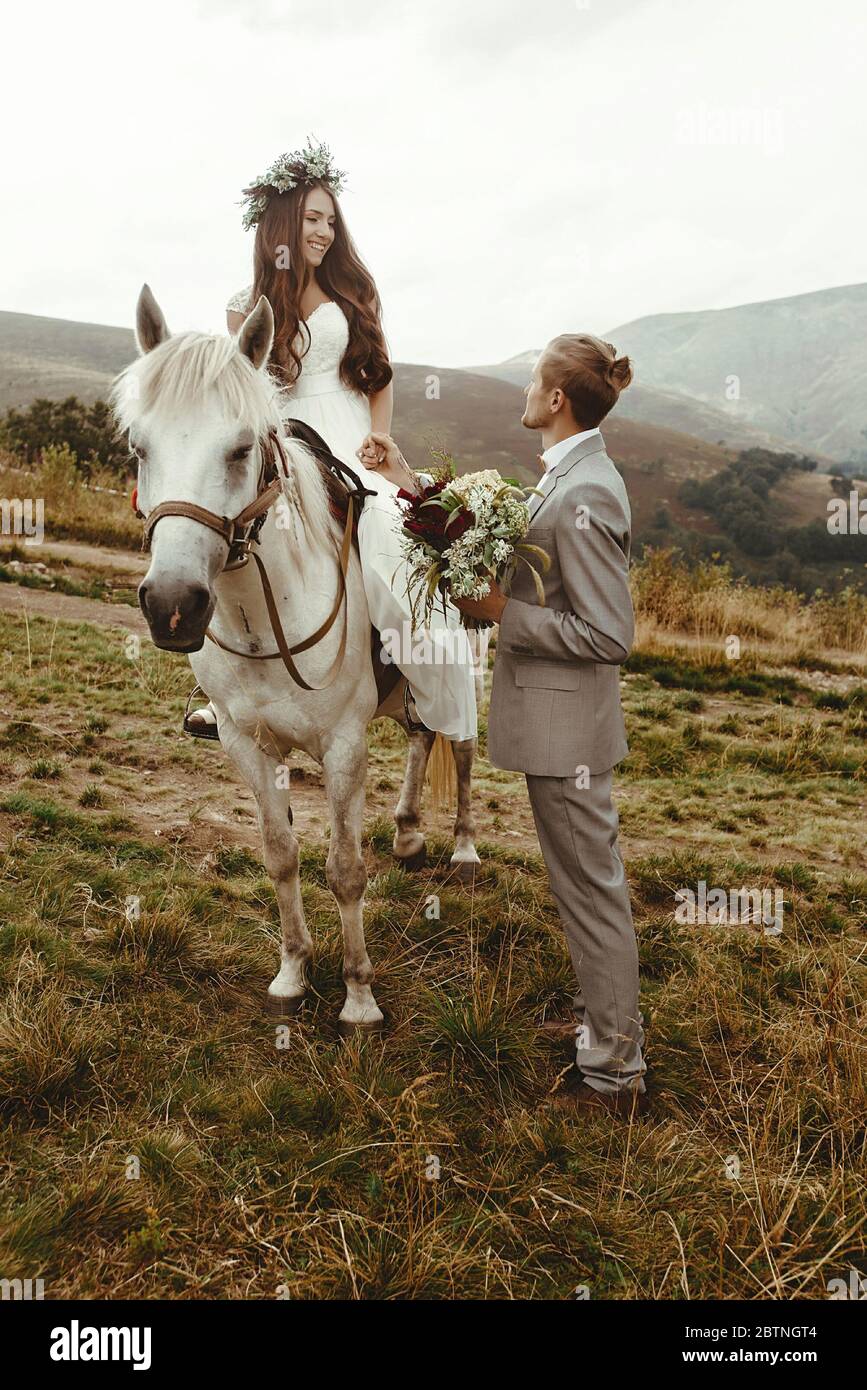 gorgeous bride riding a white horse and stylish groom, boho wedding ...