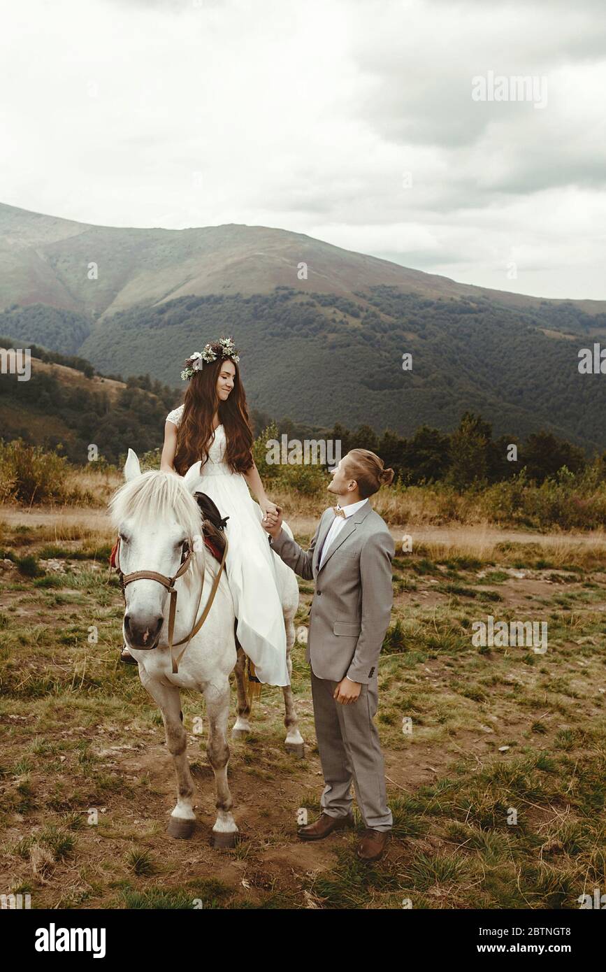 gorgeous bride riding a white horse and stylish groom, boho wedding ...