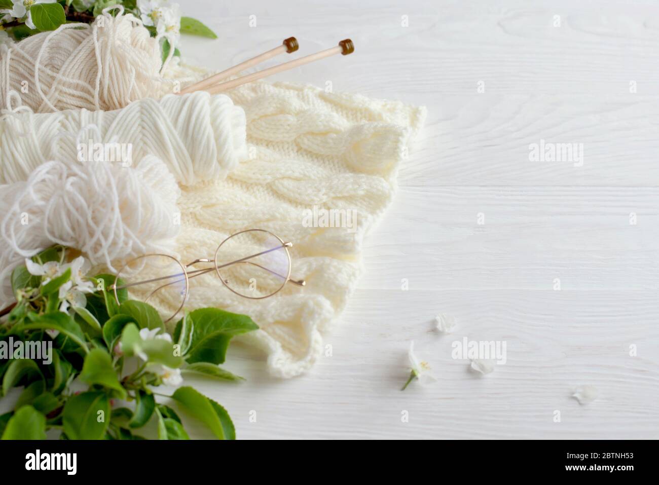 Knitting, knitting needles, yarn and glasses lie on a white wooden ...