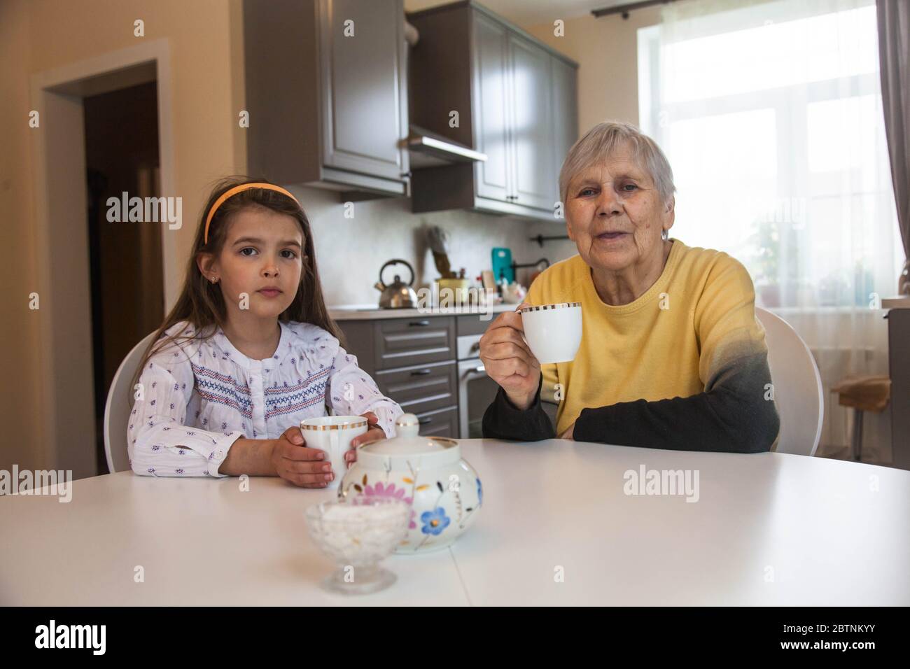 Grandmother and granddaughter drink tea sitting at the white table in ...