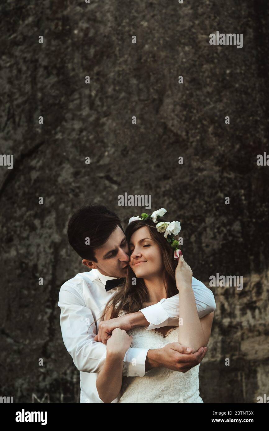 happy elegant groom hugging and kissing stylish boho bride at sunset in ...