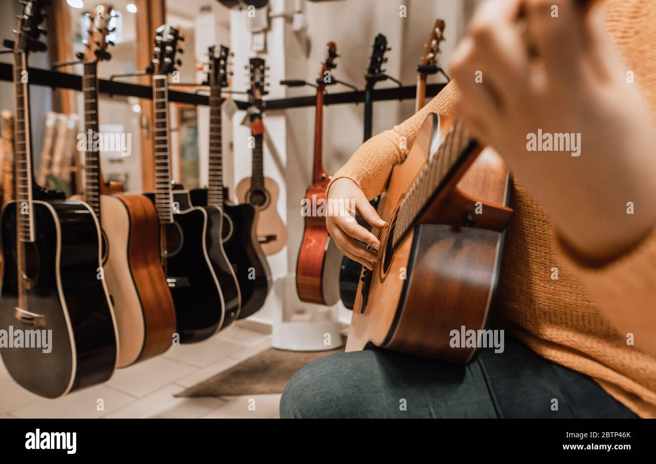 Woman musician choosing the new guitar in the musical instrument store ...