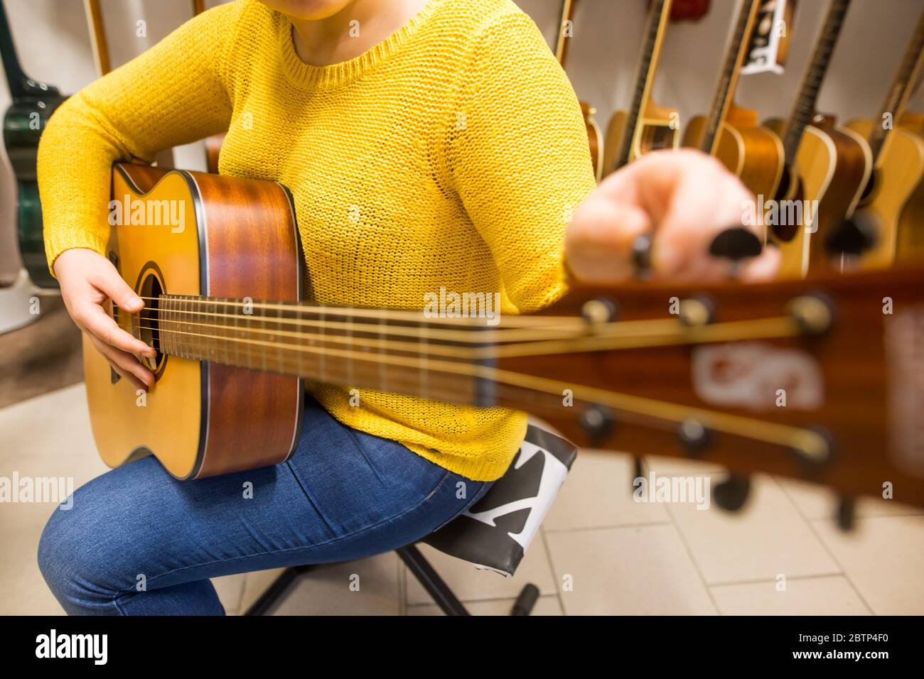 Woman musician choosing the new guitar in the musical instrument store ...