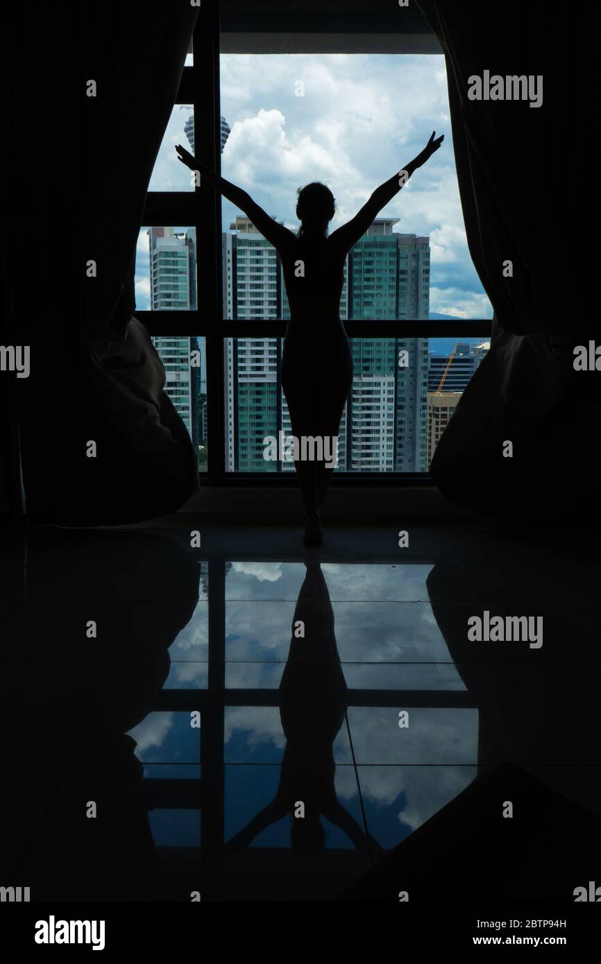 A slender girl is looking at the city through a large window. High ...