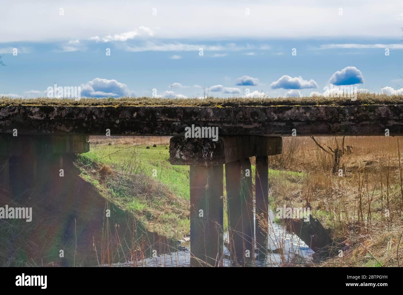 An old dilapidated bridge connects the road over a stream. Blue sky ...