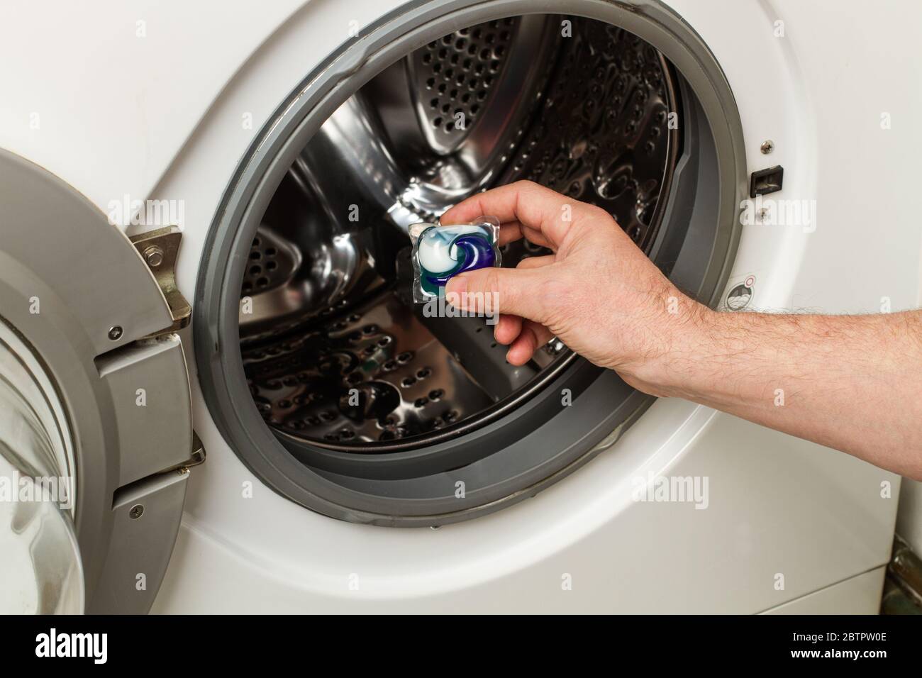 Man holding a laundry pod in front of a washing machine door Stock ...