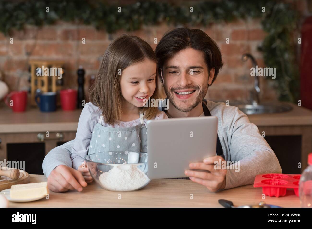 Little girl and her dad using digital tablet in kitchen, checking ...