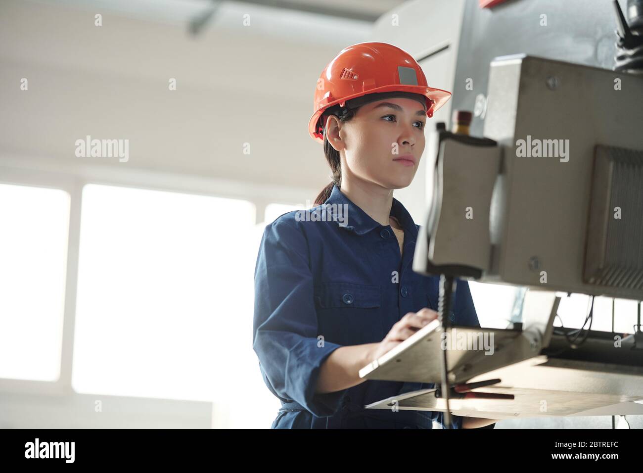 Serious young Asian operator in hardhat using computer of industrial ...