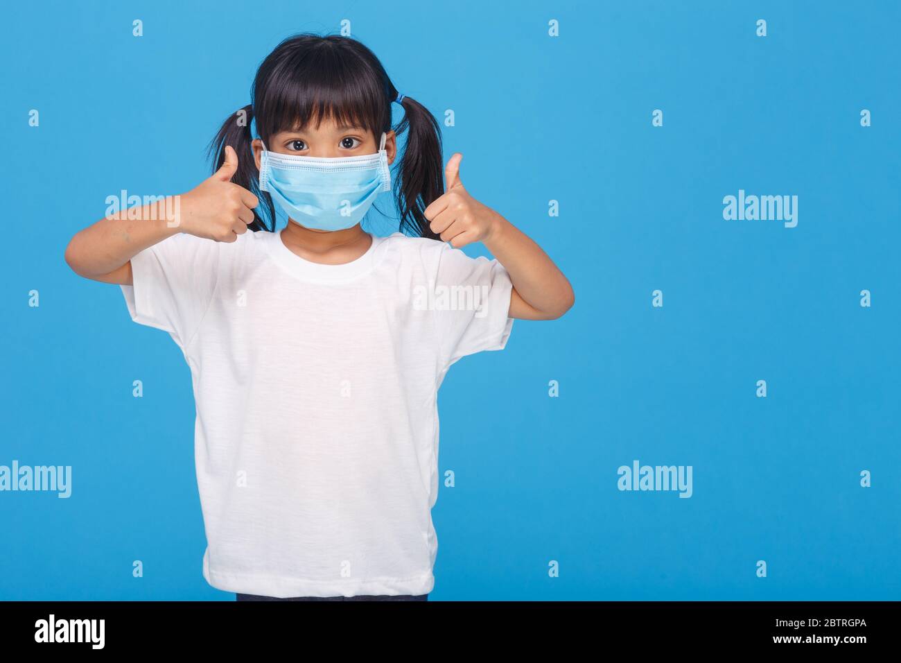 Little asian girl wearing mask for protect pm2.5 and show thumbs up gesture for good air outdoor ...