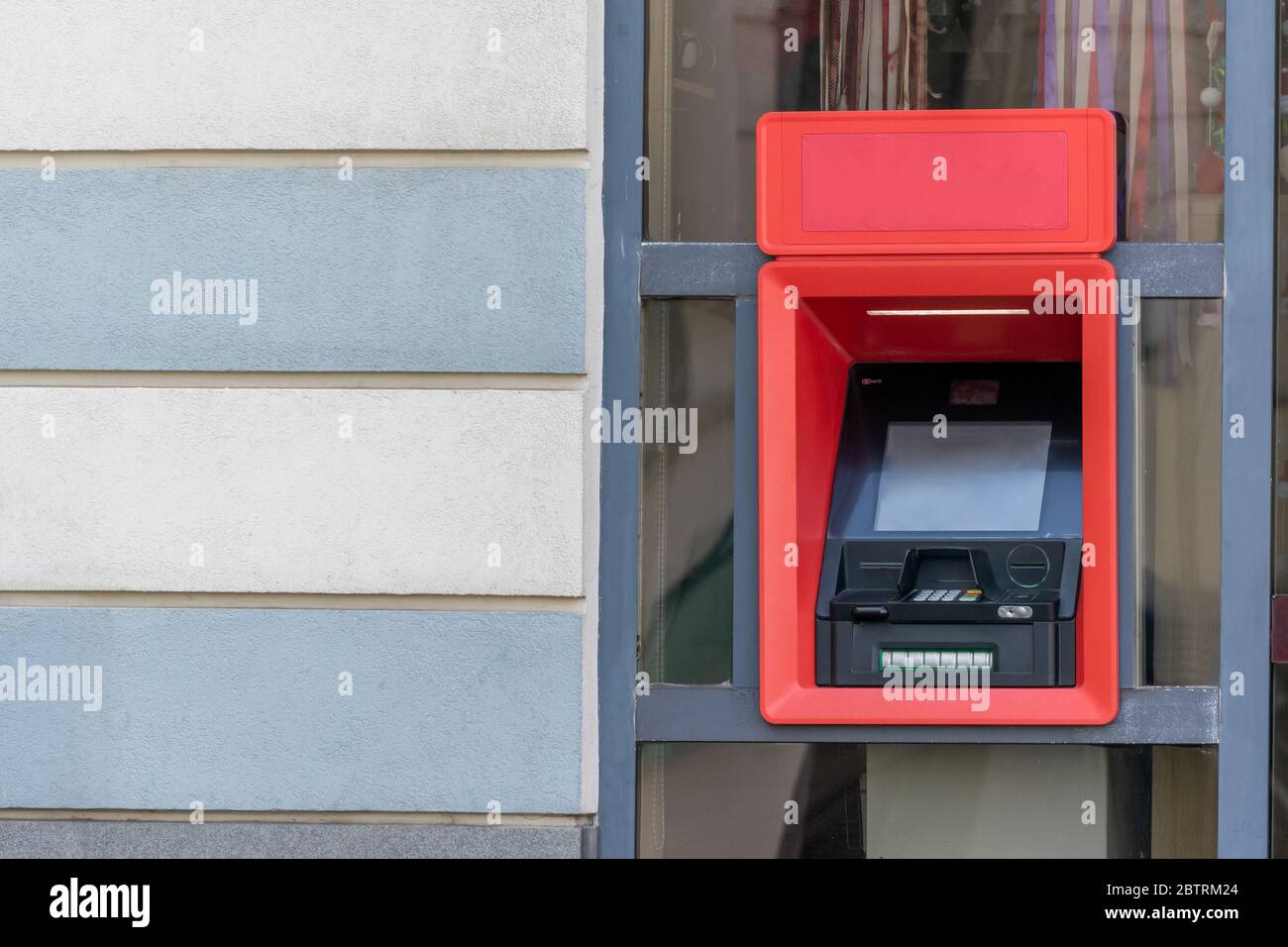 A red ATM is embedded in the wall of the building. Automated Teller Machine in the city street ...