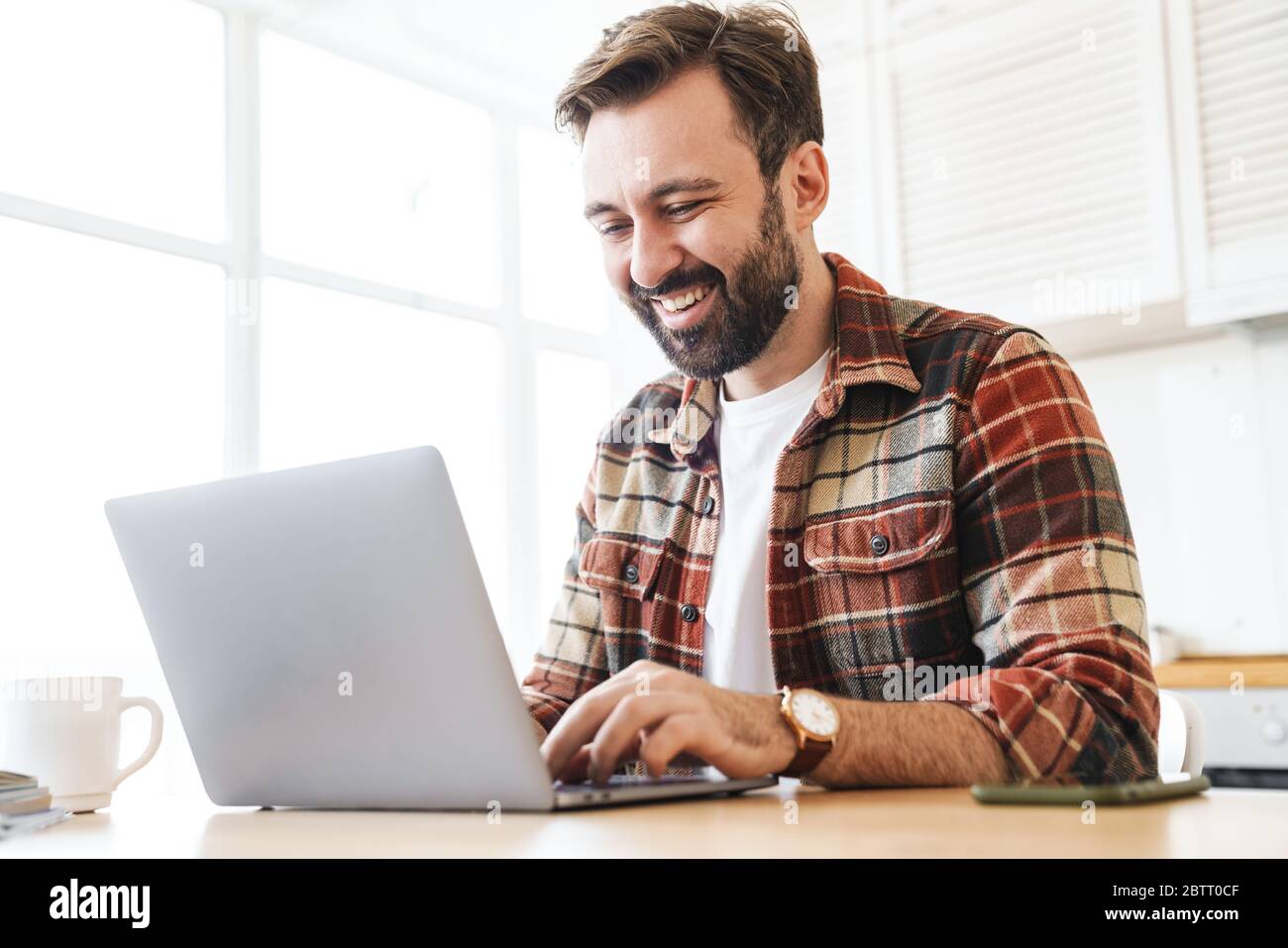 Portrait of cheerful bearded man working with laptop and smiling while ...