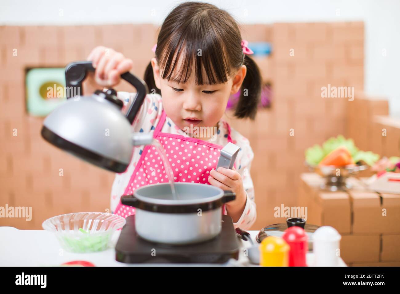 toddler girl pretend play food preparing role against cardboard blocks ...