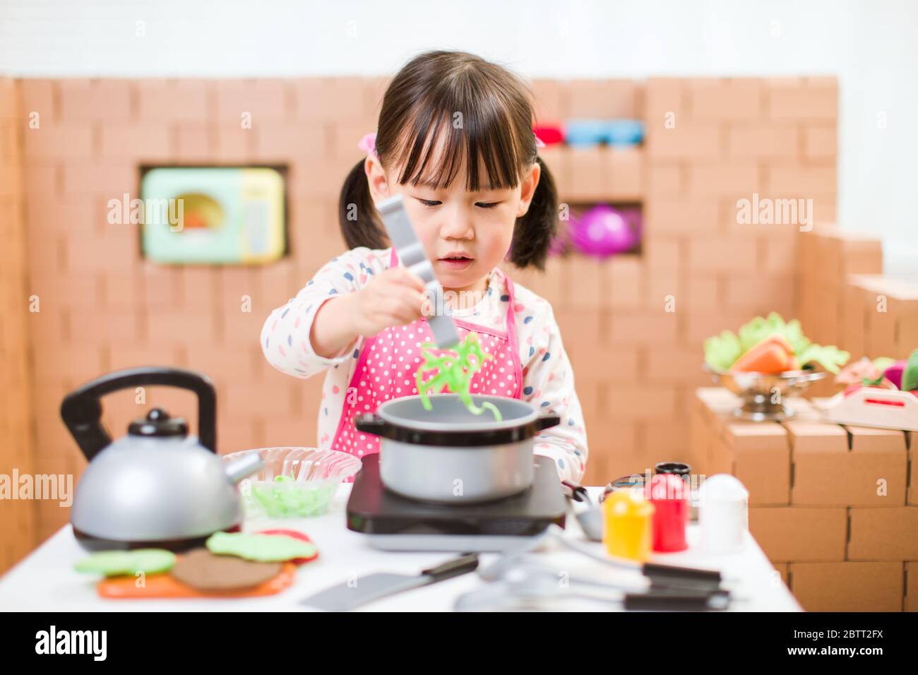 toddler girl pretend play food preparing role against cardboard blocks ...