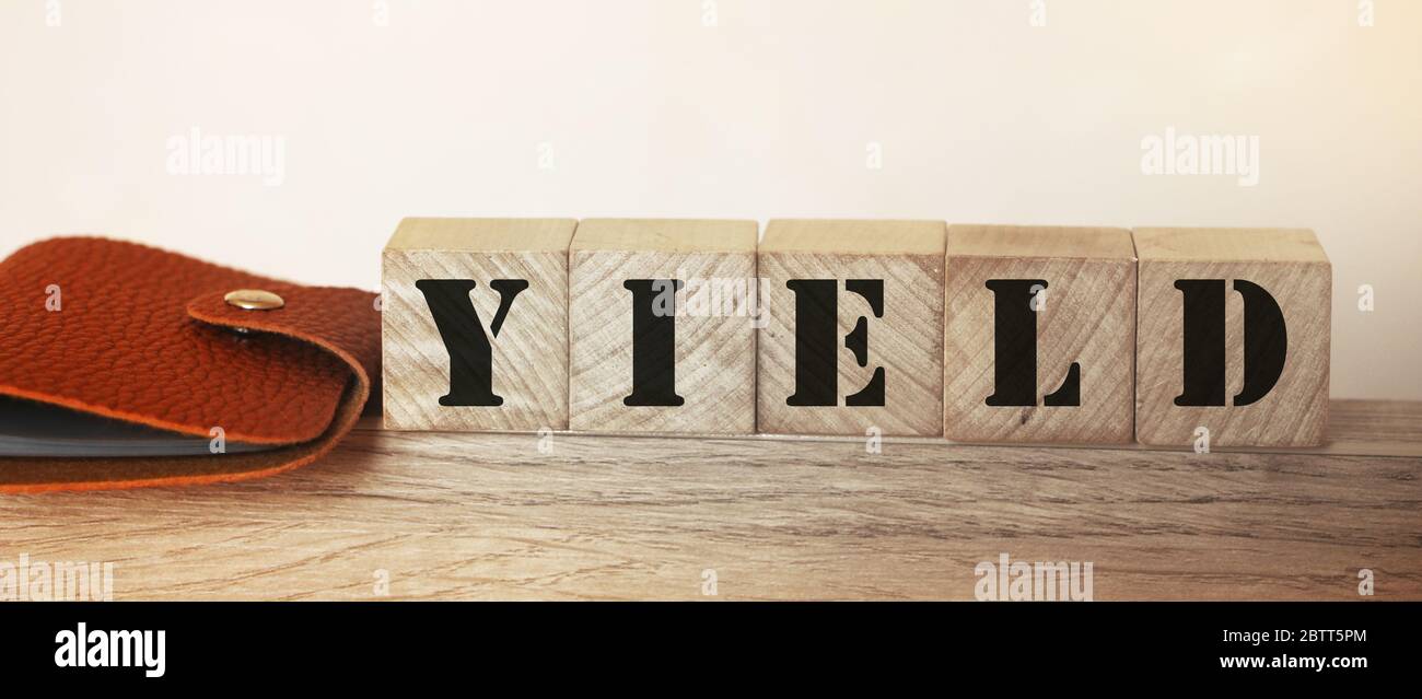 Yield Word on Wooden Cubes and brown leather wallet on wooden table ...